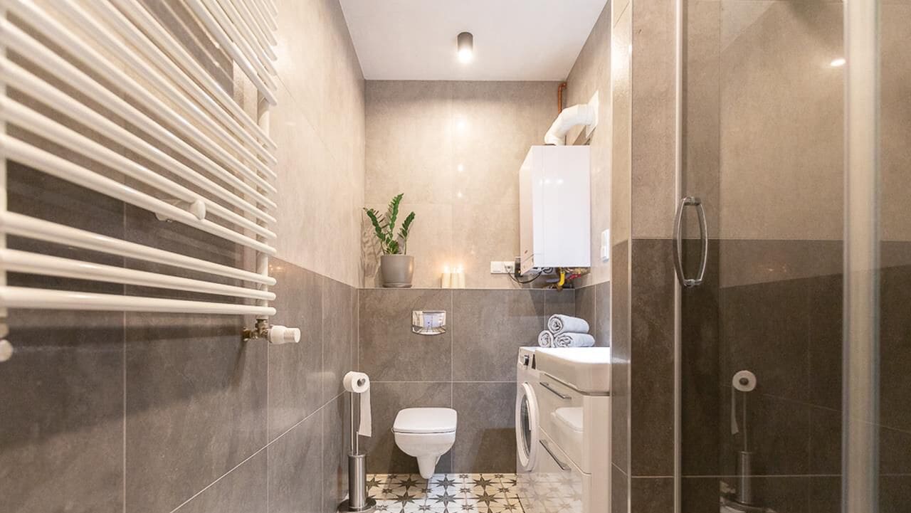 Uma casa de banho moderna com chuveiro, sanita e máquina de lavar roupa.
