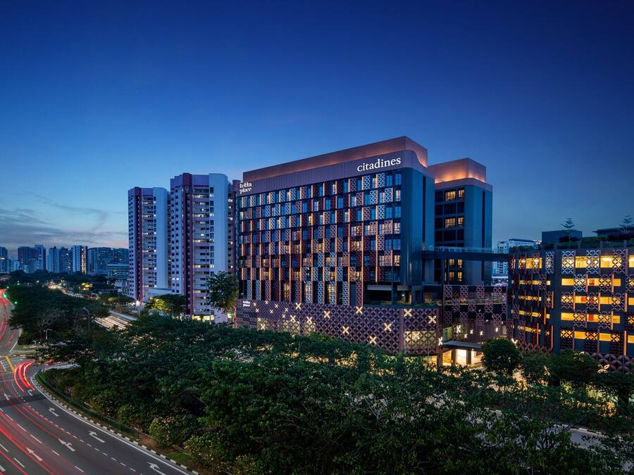 Um hotel moderno com um letreiro de 'citadines' em destaque, rodeado por edifícios altos e uma rua bem iluminada.