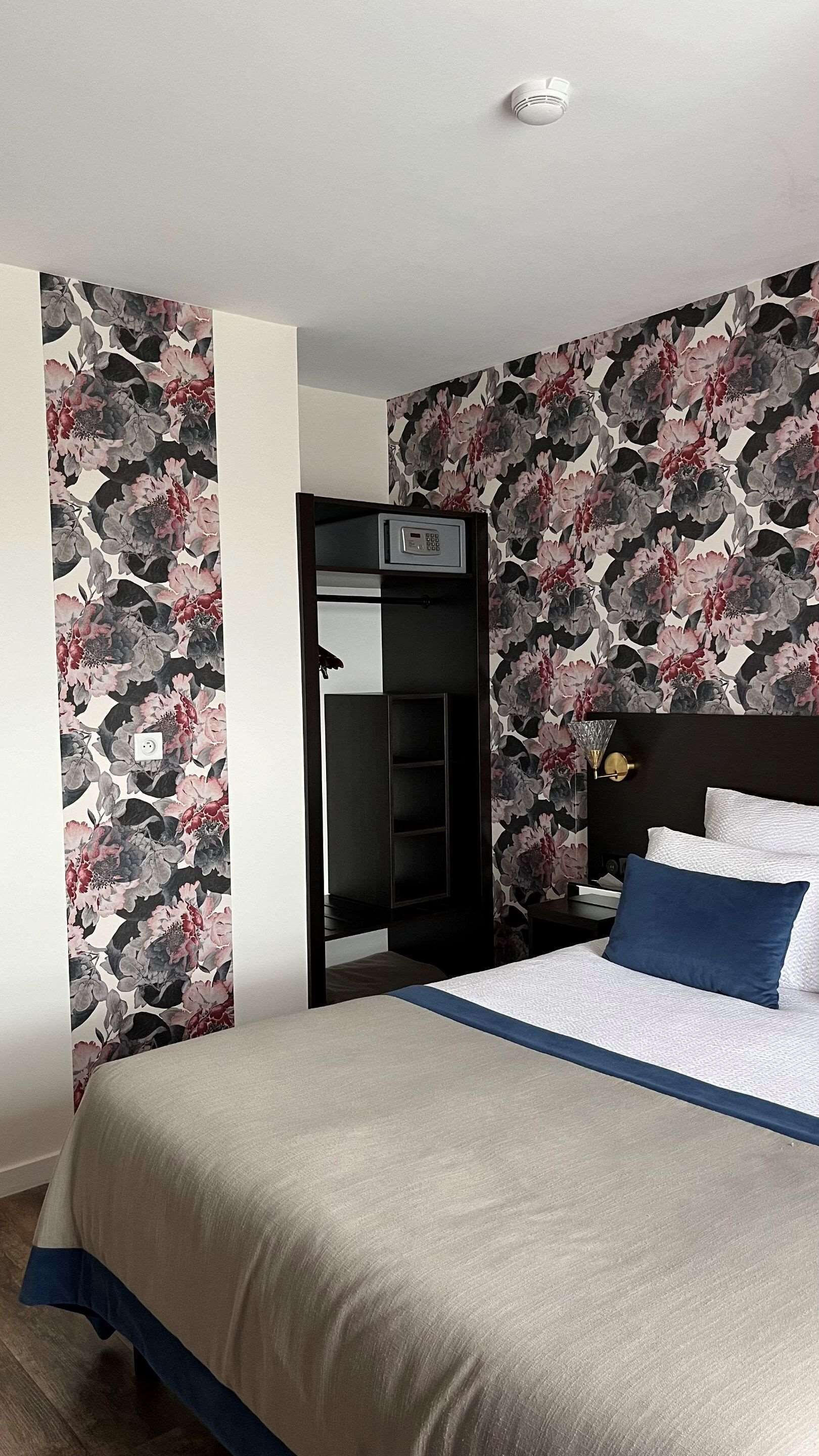 Quarto de hotel com uma cama, mesa de cabeceira, espelho e guarda-roupa.