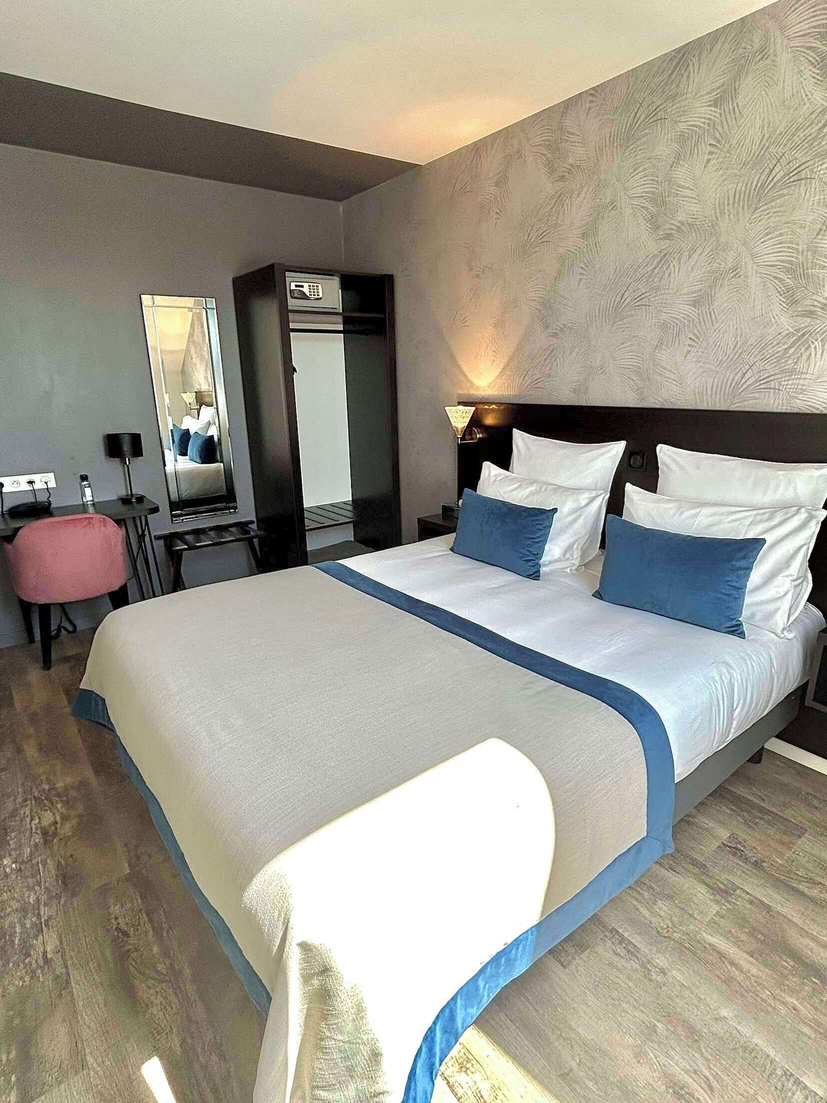 Quarto de hotel moderno com uma cama grande, mesa de cabeceira, espelho e guarda-roupa.