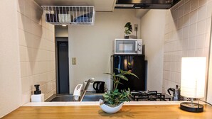 Cozinha compacta com micro-ondas, geladeira, pia e um vaso de planta no balcão.