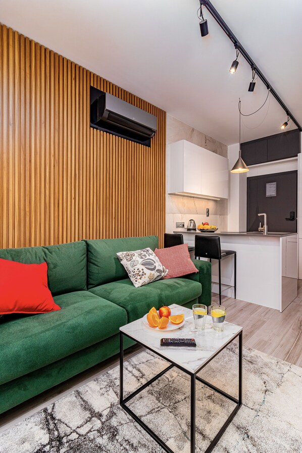 Uma sala de estar moderna com um sofá verde, uma mesa de centro e uma área de cozinha com bancada e armários.