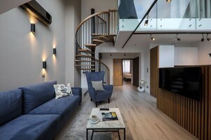 Uma sala de estar moderna com um sofá azul, uma mesa de centro com uma revista, uma poltrona azul e uma escada em espiral.