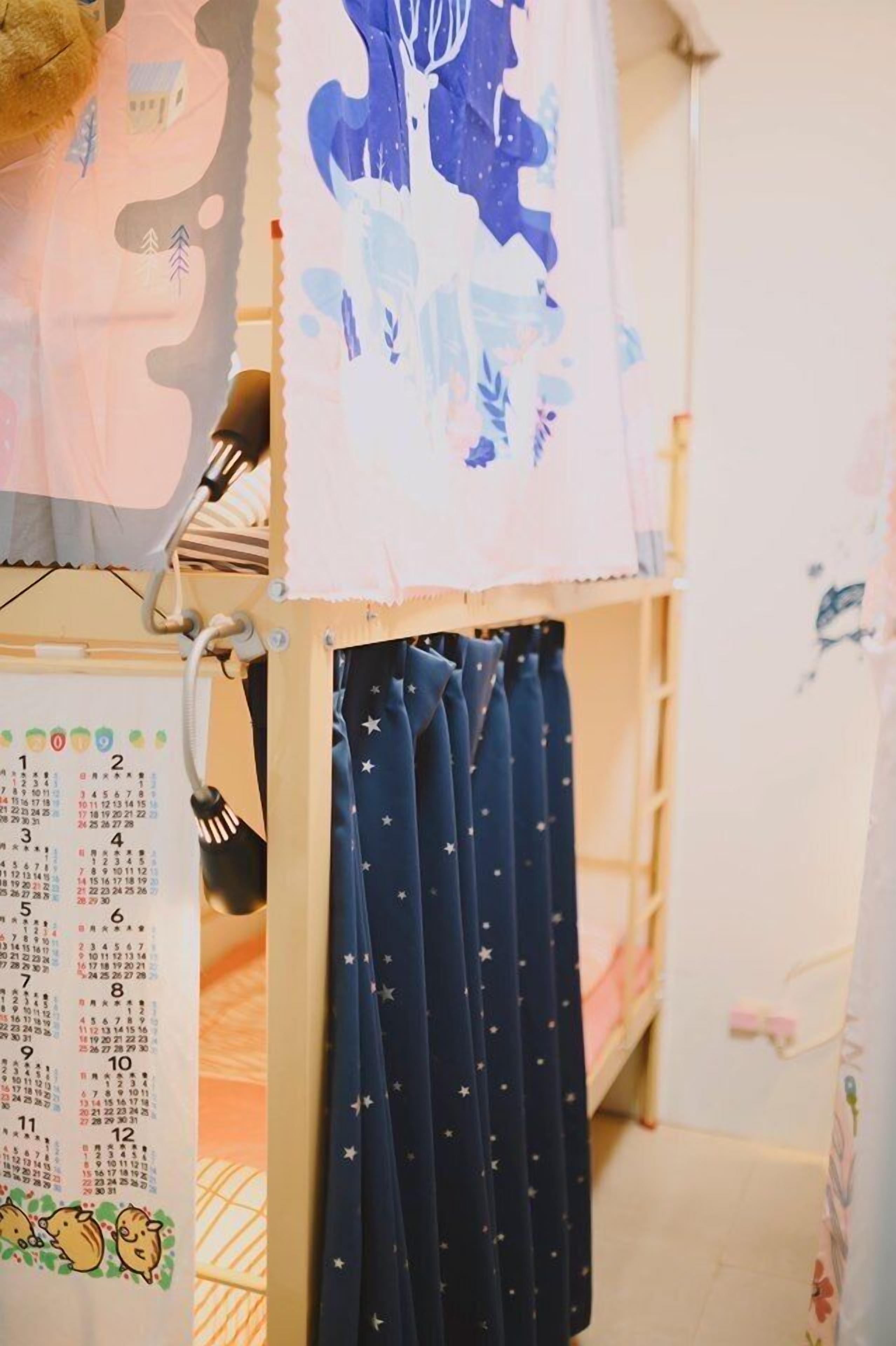 Uma cama de beliche com um calendário na lateral, uma cortina com padrão de estrelas e uma pequena prateleira com um ursinho de pelúcia.