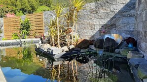 Uma área de piscina ao ar livre tranquila, com um muro de pedra, cerca de madeira e diversas plantas.