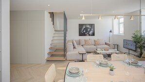Uma sala de estar moderna com escada, sofá, mesa de jantar posta para quatro e televisão.