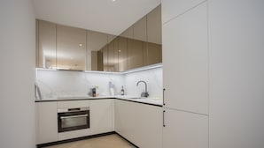 Uma cozinha moderna com armários brancos, bancada de mármore e forno embutido.