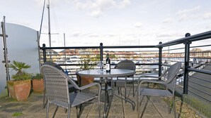 Terraço com mesa redonda e quatro cadeiras, com vista para uma marina com barcos.
