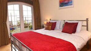 Quarto com uma cama grande, vista para o jardim através de uma porta deslizante e um quadro na parede.