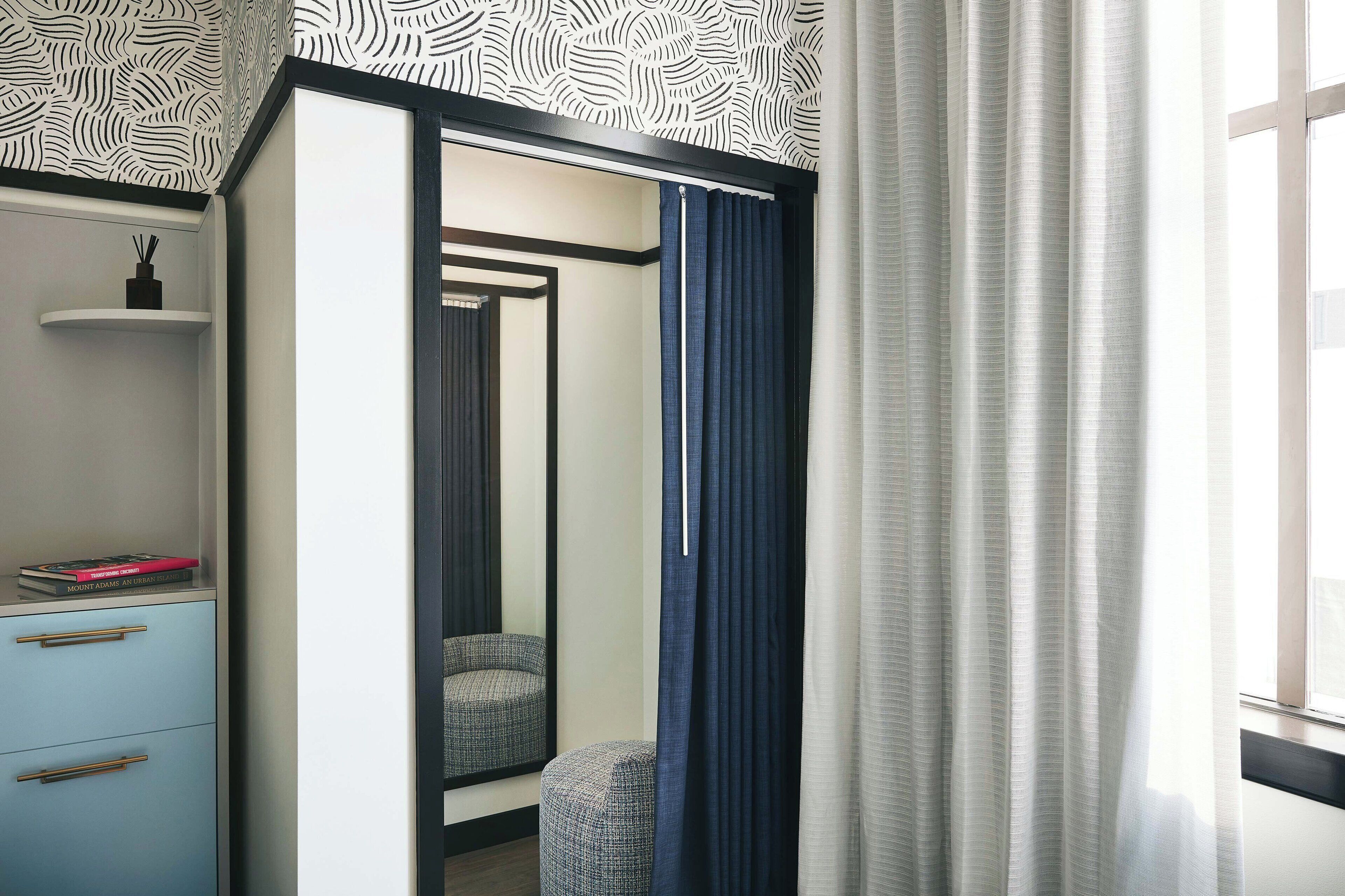 Quarto com guarda-roupa, mesa de cabeceira, cadeira e janela com cortinas.