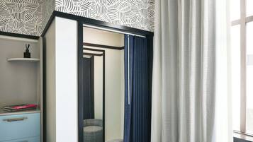 Quarto com guarda-roupa, mesa de cabeceira, cadeira e janela com cortinas.