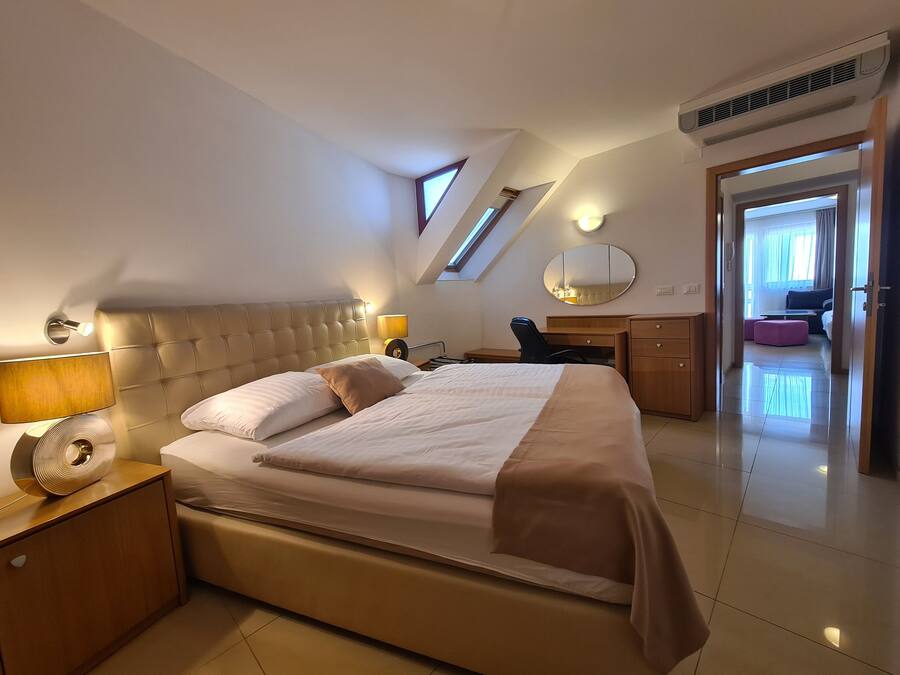 Quarto de hotel com uma cama grande, uma escrivaninha, uma cadeira, um espelho e um claraboia.