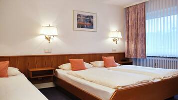 Quarto de hotel com duas camas, cabeceira de madeira, duas mesas de cabeceira, um criado-mudo, luminária na parede, janela com cortinas e um quadro na parede.