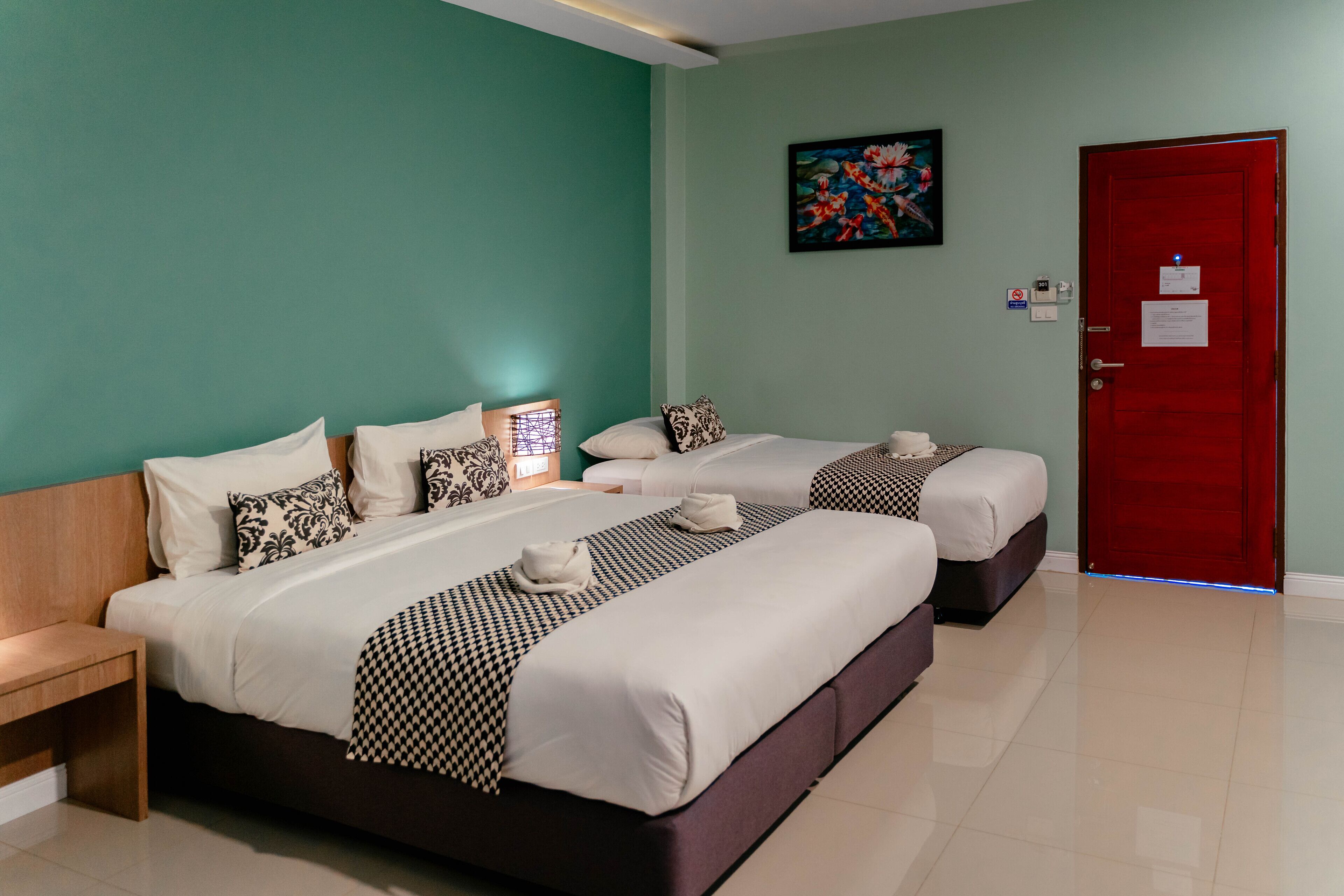 Quarto de hotel com duas camas, uma mesinha de cabeceira, uma porta vermelha e um quadro com flores na parede.