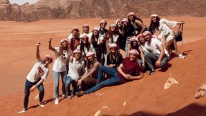 Um grupo de pessoas posando em uma paisagem desértica com formações rochosas ao fundo.