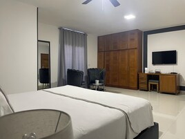 Quarto de hotel com cama, escrivaninha, cadeira, guarda-roupa, televisão e ventoinha no teto.
