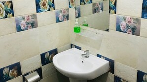 Um banheiro com pia branca, espelho e azulejos estampados com motivos florais.