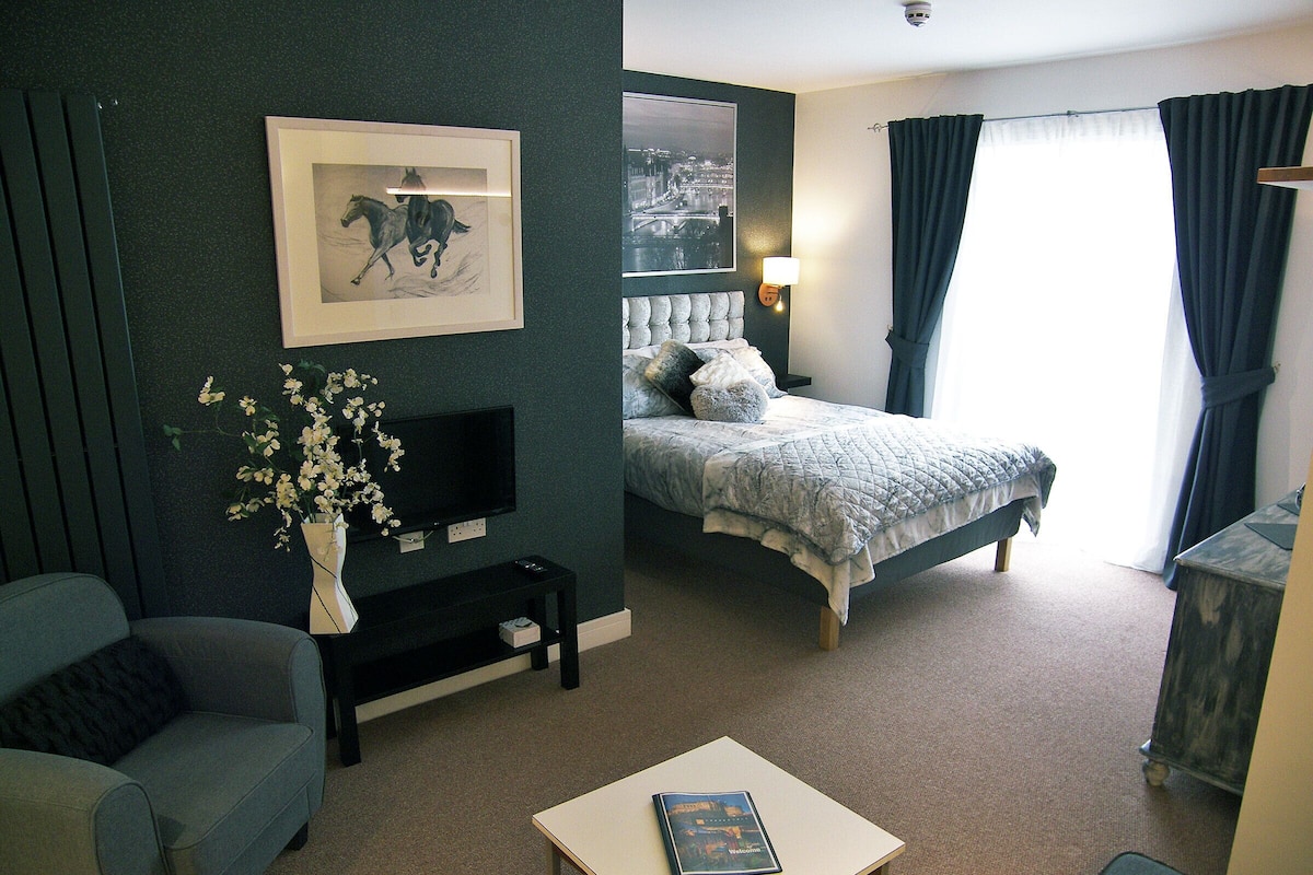 Quarto de hotel com cama, televisão, sofá e mesa de centro.
