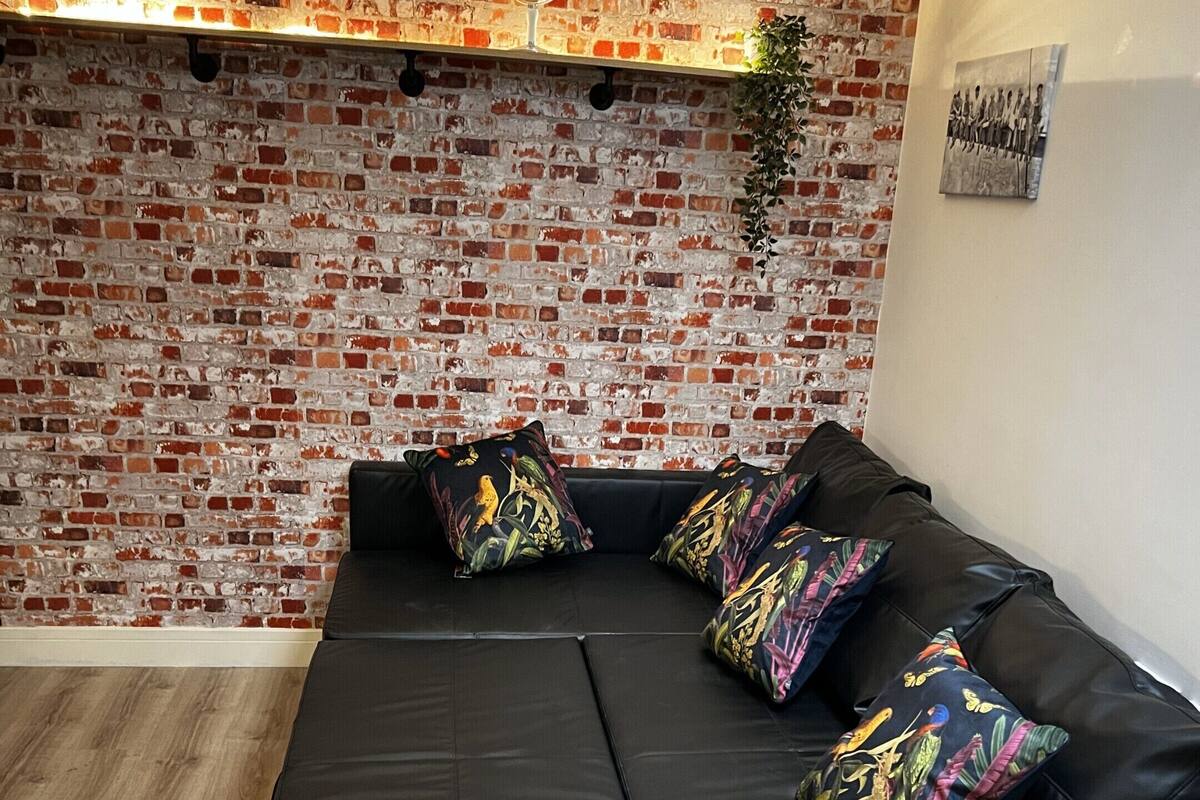 Um sofá modular preto com almofadas coloridas em frente a uma parede de tijolos.