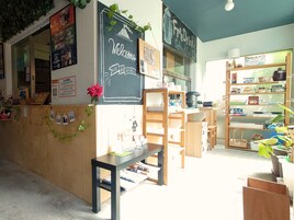 Interior acolhedor de uma cafeteria com um quadro-negro com a inscrição 'Welcome', móveis de madeira e prateleiras repletas de diversos artigos.