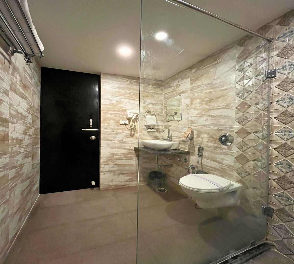 Um banheiro moderno com box de vidro, porta preta e parede revestida com padrões geométricos.