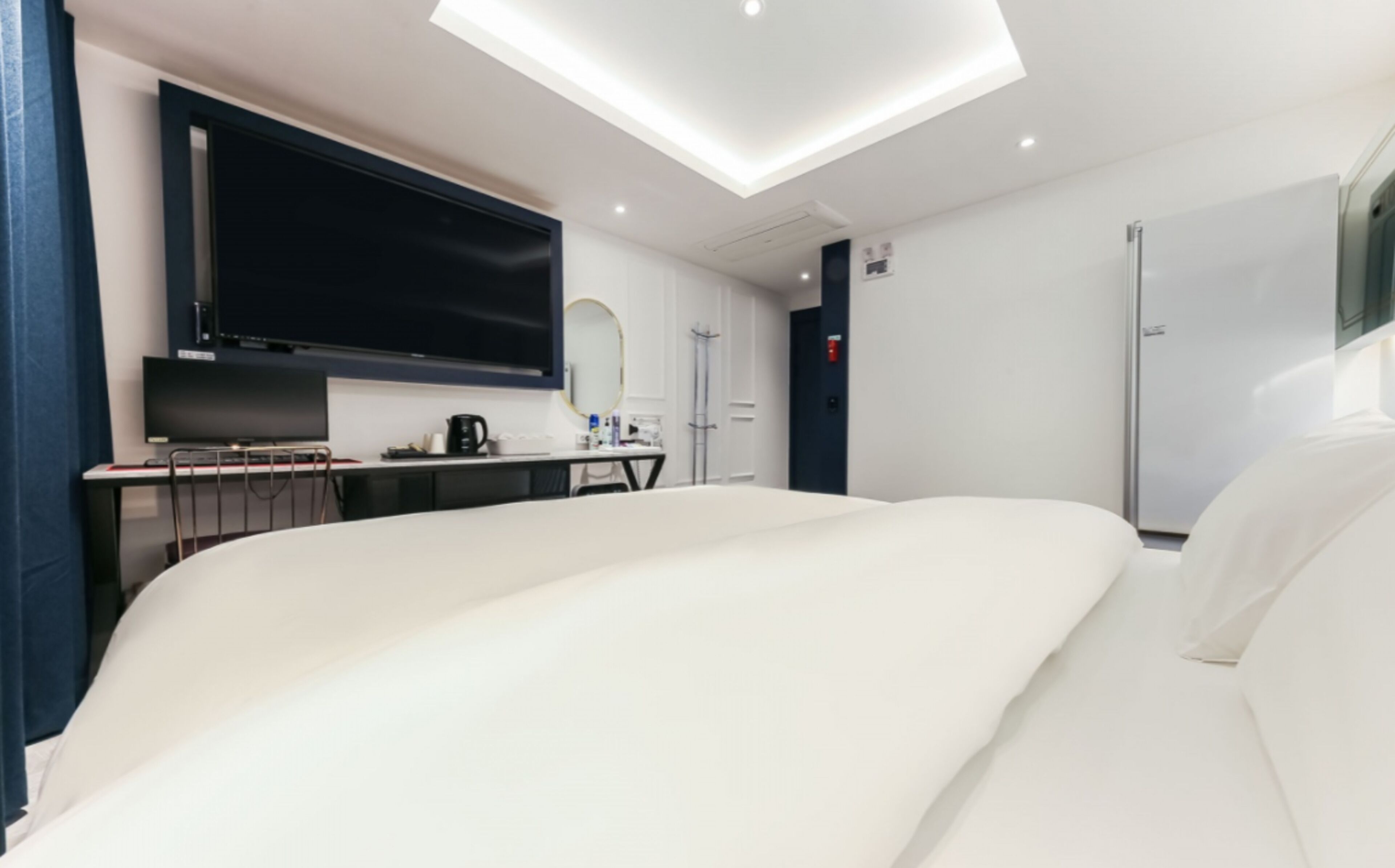Quarto de hotel moderno com uma cama grande, uma escrivaninha com computador, uma televisão de tela plana e um guarda-roupa.