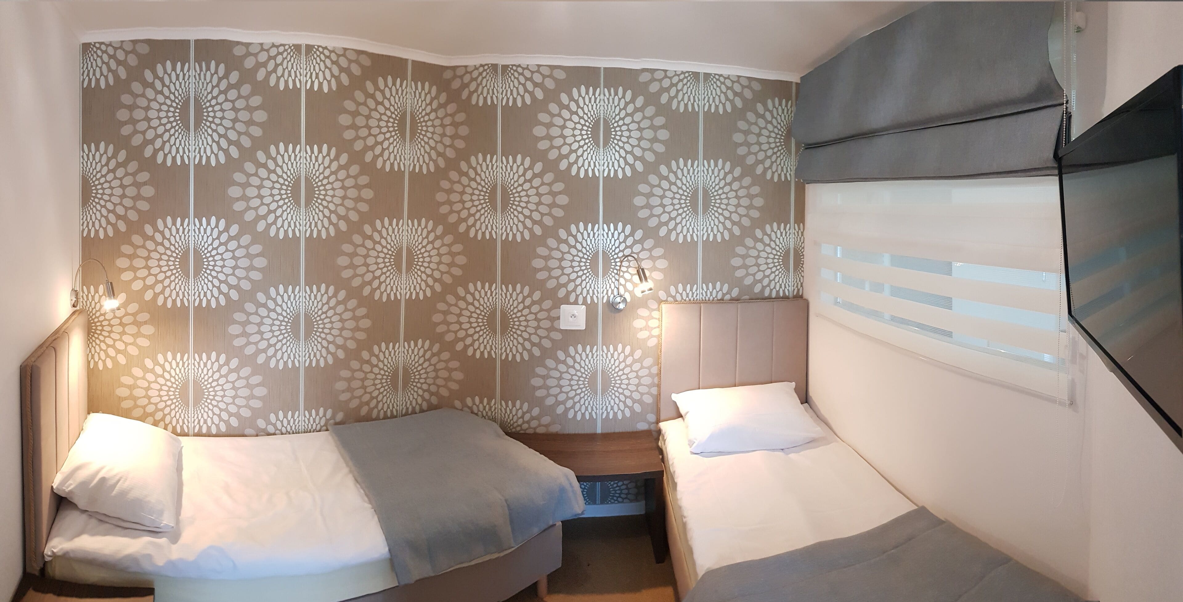 Quarto com duas camas, parede estampada e janela com persianas.