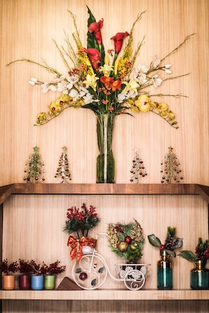 Uma prateleira de madeira com um arranjo floral, pequenas árvores de Natal e vários vasos de plantas.