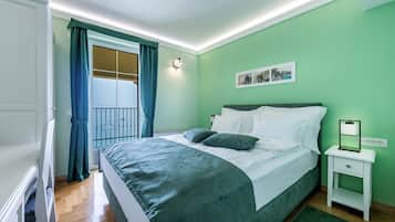 Um quarto com uma cama, uma mesinha de cabeceira, parede verde, janela com cortinas e um quadro na parede.