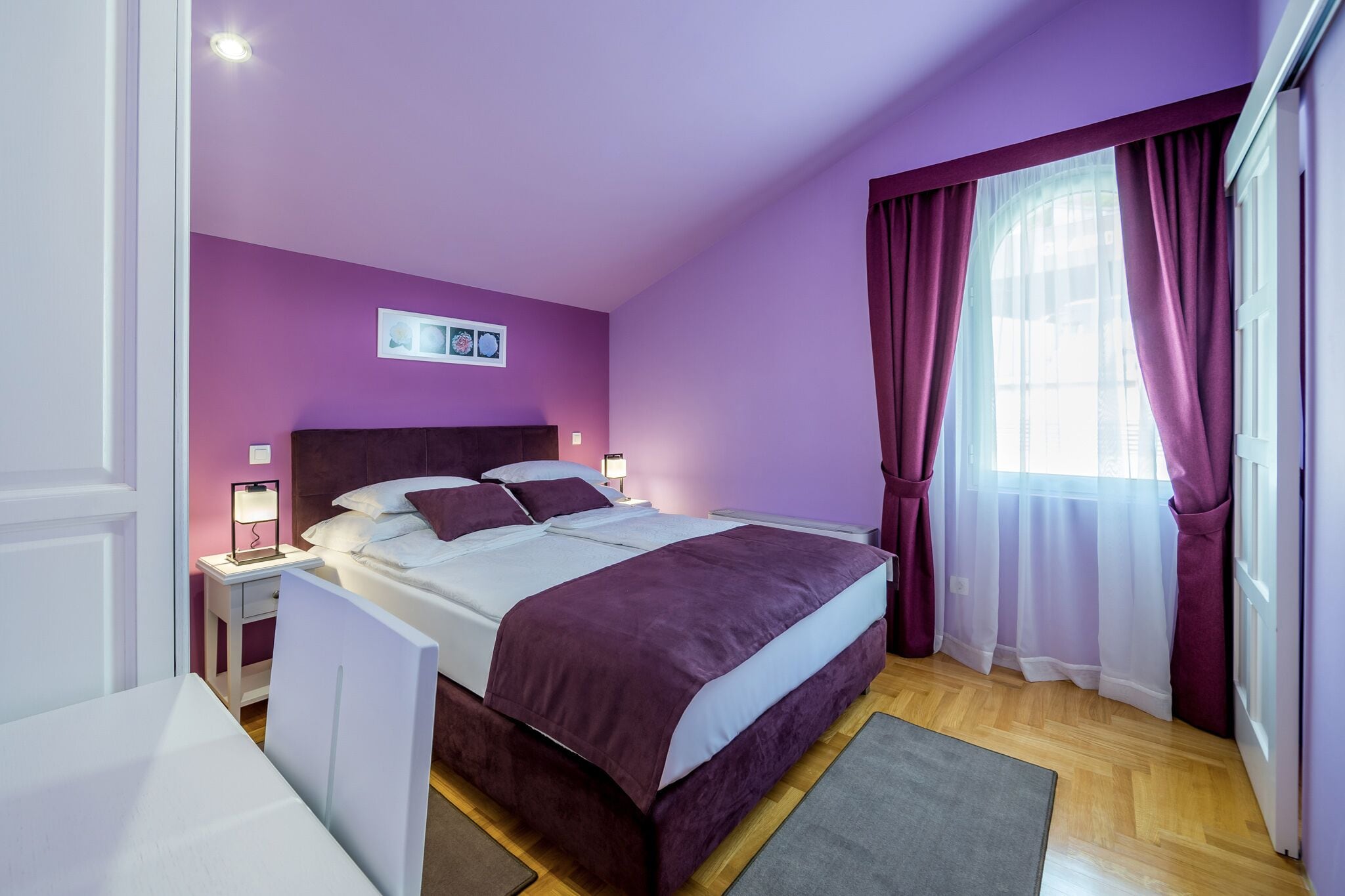 Quarto com cama grande, mesa de cabeceira, abajur e janela com cortinas.