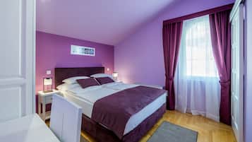 Quarto com cama grande, mesa de cabeceira, abajur e janela com cortinas.