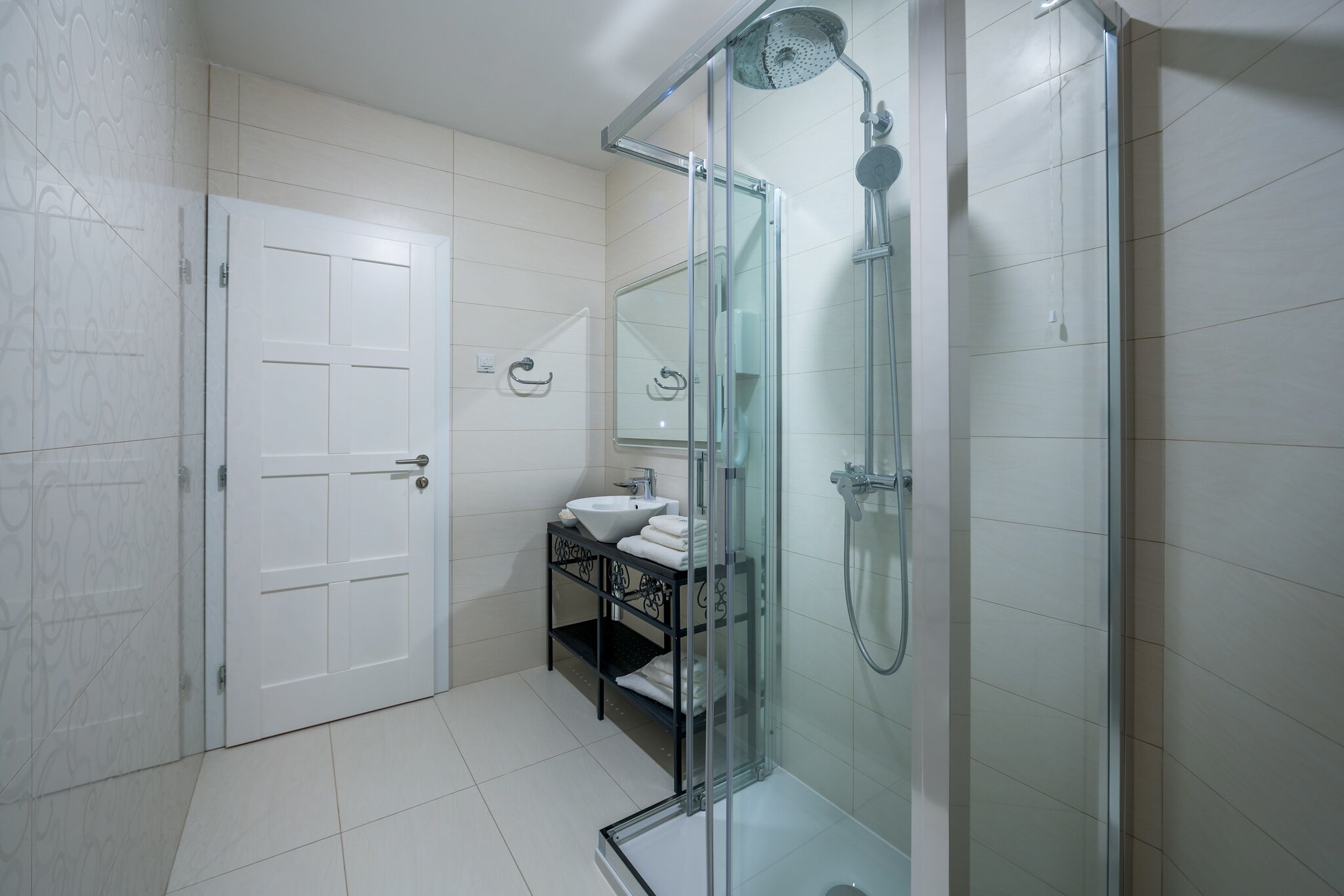 Casa de banho moderna com chuveiro de vidro, porta branca e toucador com lavatório e barra de toalhas.