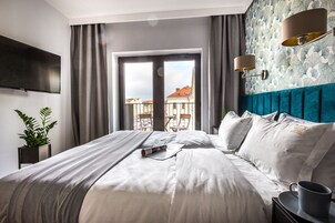 Cama bem arrumada com vista para edifícios pela janela, televisão de tela plana na parede e um vaso de planta.