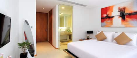 Quarto de hotel com cama, televisão, quadro e banheiro visível através de uma porta de vidro.