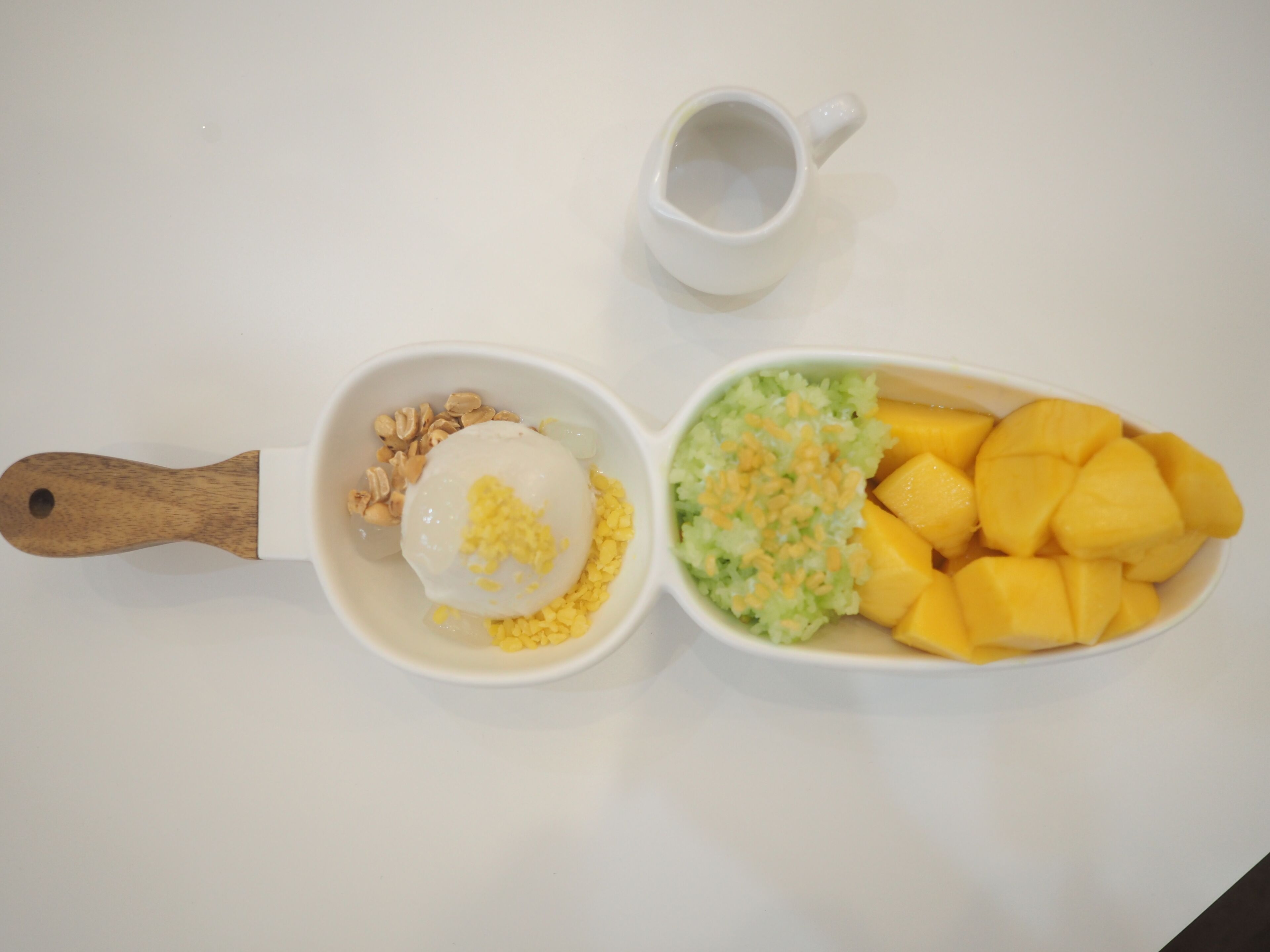 Uma mesa branca com um recipiente de madeira e uma colher cheia de um pó branco, uma xícara branca e uma tigela com pedaços amarelos e arroz verde.