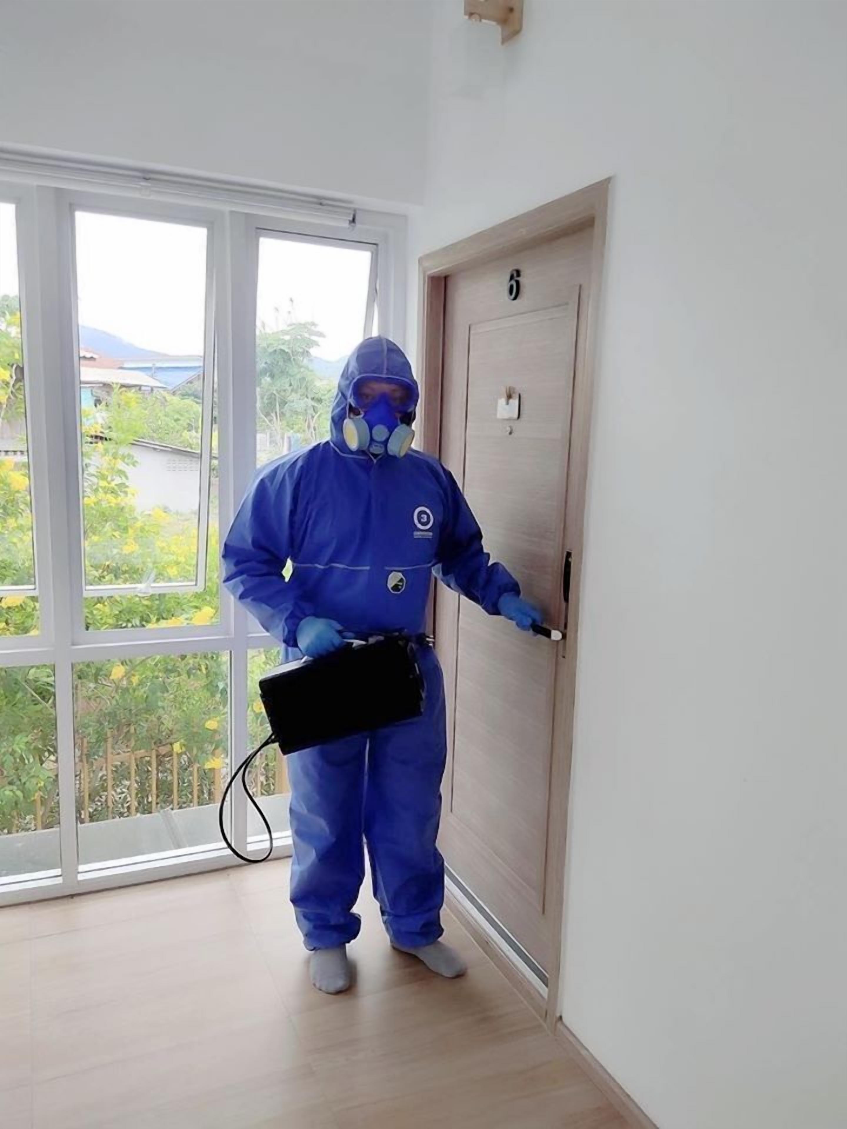 Uma pessoa num fato azul de proteção está numa sala com porta de madeira e janelas grandes.