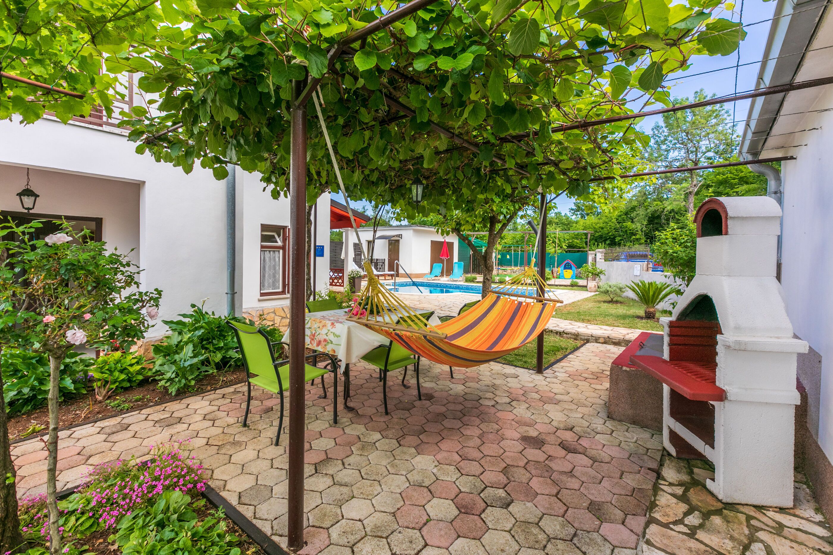 Uma área de pátio com uma rede, churrasqueira e piscina ao fundo.
