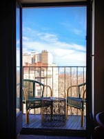 Varanda com cadeiras de vime e uma mesa, com vista para um horizonte urbano repleto de edifícios e um céu claro.