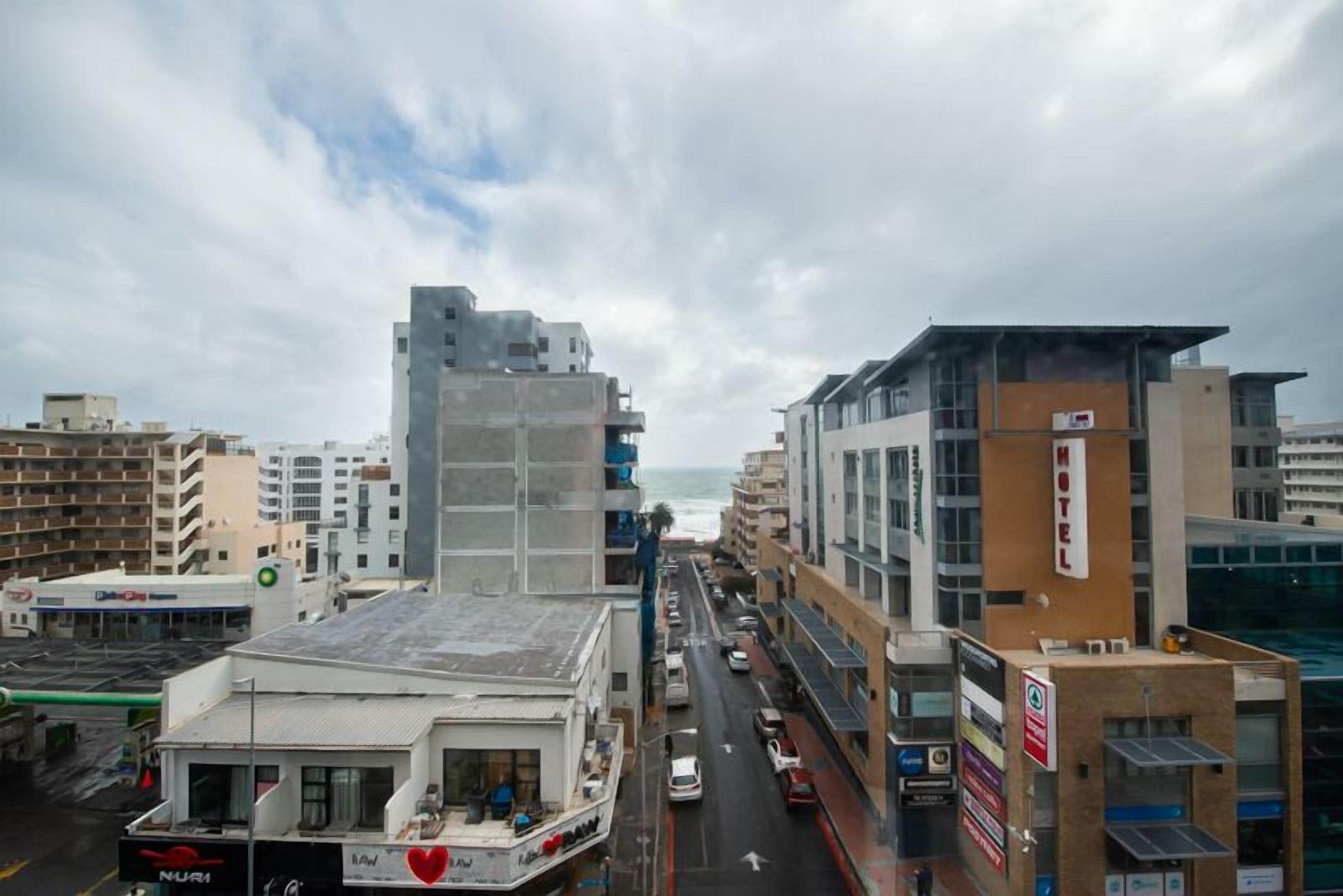 Paisagem urbana costeira com um hotel em destaque, design moderno, rua movimentada com veículos e vista para o oceano.