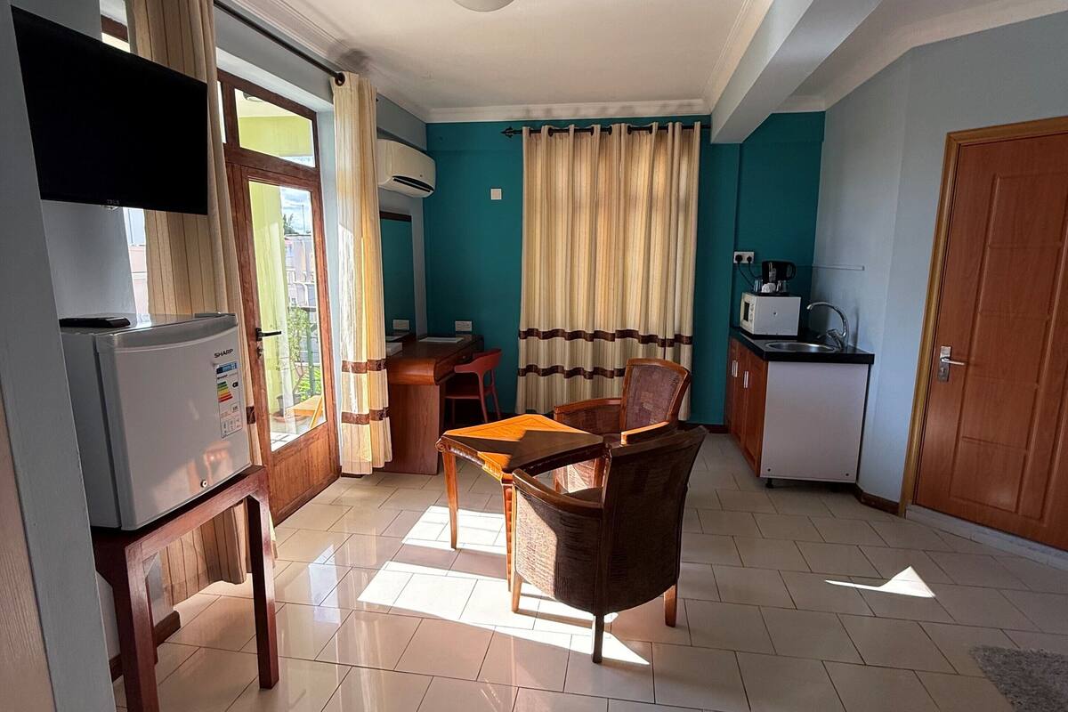 Um espaço compacto com cozinha compacta, área de refeições com mesa e cadeiras, televisão fixada na parede e janela com cortinas.
