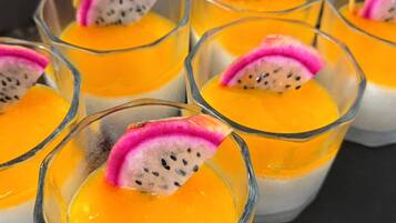 Vários copos de vidro transparente com sobremesa amarela e guarnição de fruta rosa.