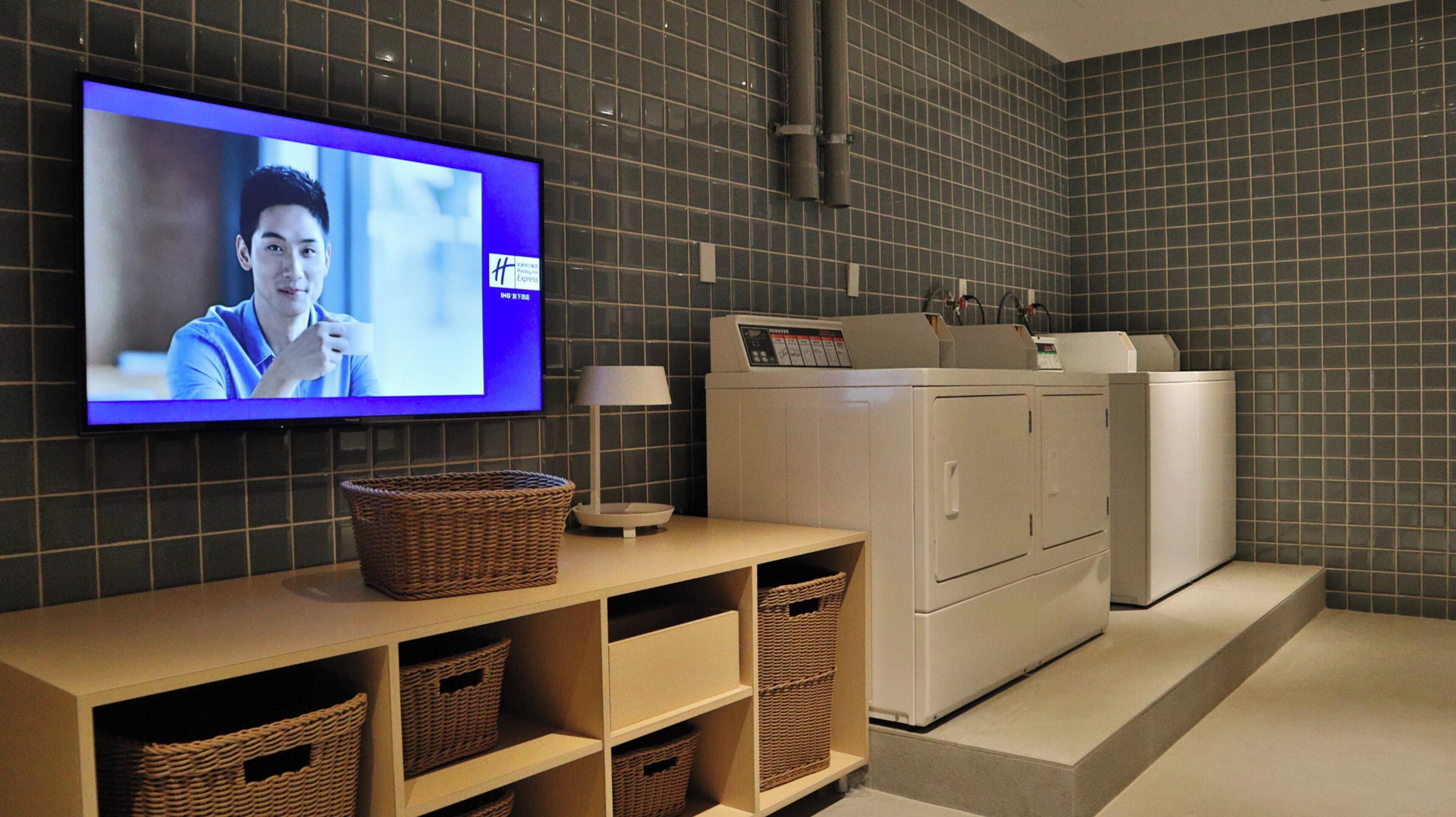 Uma casa de banho moderna com televisão na parede, máquina de lavar e cestos de vime numa estante de madeira.