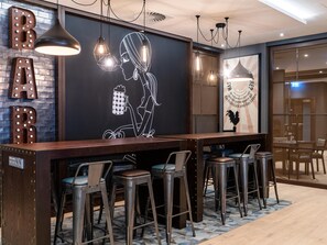 Uma área de bar com um mural, luminárias pendentes e banquetas.