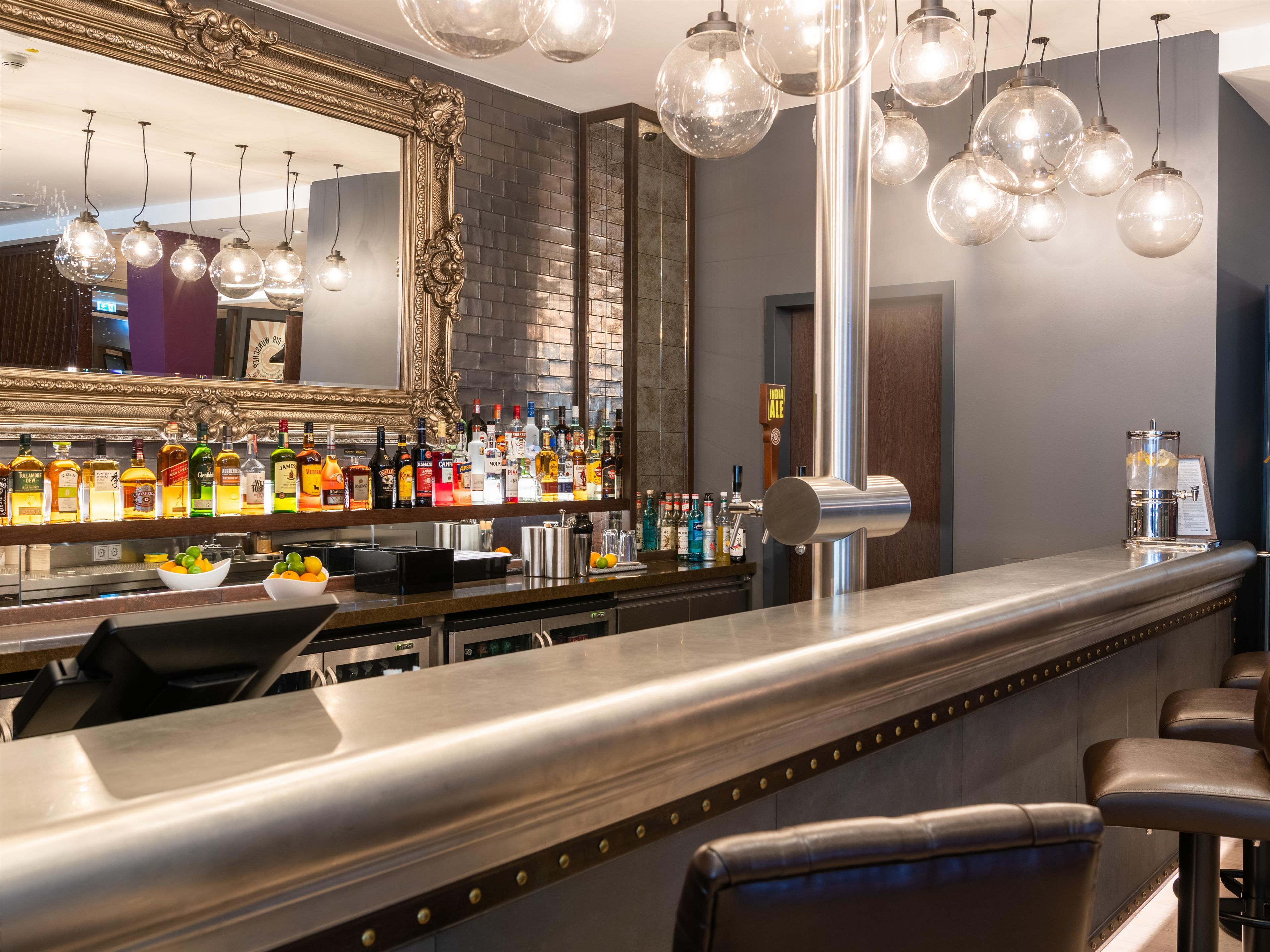 Uma área de bar com espelho, luminárias esféricas pendentes e diversos tipos de bebidas.