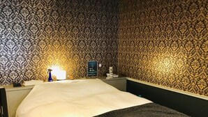 Quarto de hotel com uma cama grande, uma mesa de cabeceira com luminária e um papel de parede estampado.