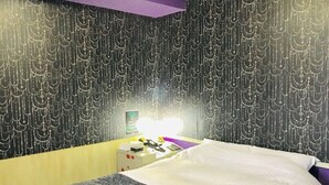 Quarto de hotel com cama, mesa de cabeceira e luminária, e parede com desenho decorativo.
