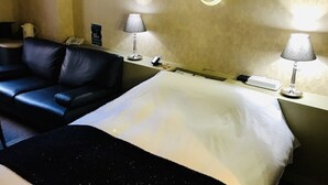 Quarto de hotel com uma cama, um sofá de couro preto, duas luminárias de cabeceira e uma TV fixada na parede.