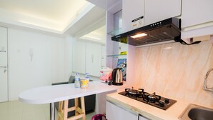 Cozinha compacta com bancada branca, fogão a gás, pia e um banquinho de madeira.
