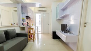Uma sala de estar moderna com um sofá cinza, um banquinho de madeira e uma TV em um armário branco.