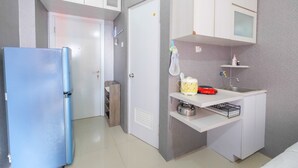 Uma cozinha compacta com geladeira, pia e pequeno balcão com chaleira e escorredor de louça.